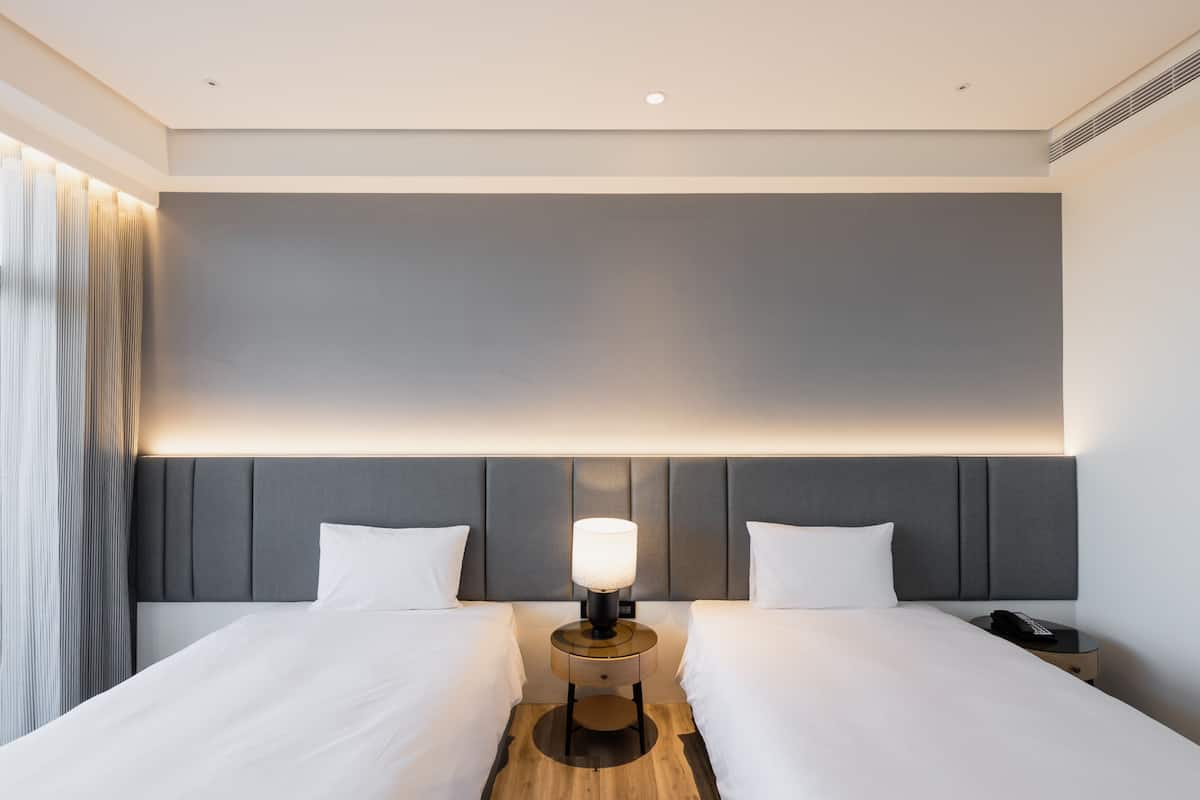 Quarto de hotel moderno, com uma cama grande, uma mesa de cabeceira com abajur e outro criado-mudo com telefone.