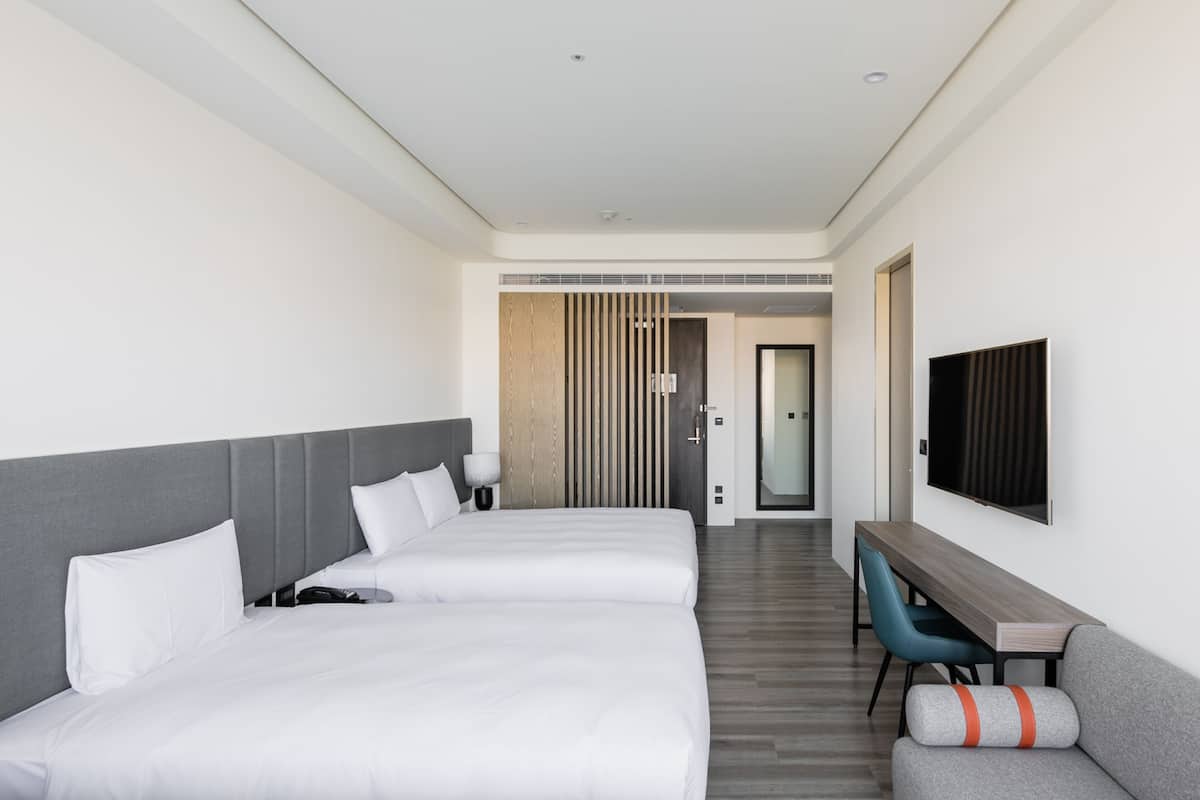 Quarto de hotel moderno com duas camas, uma mesa e uma televisão.