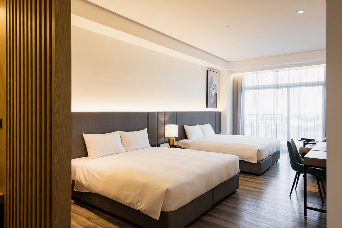 Quarto de hotel com duas camas, uma escrivaninha e uma cadeira.