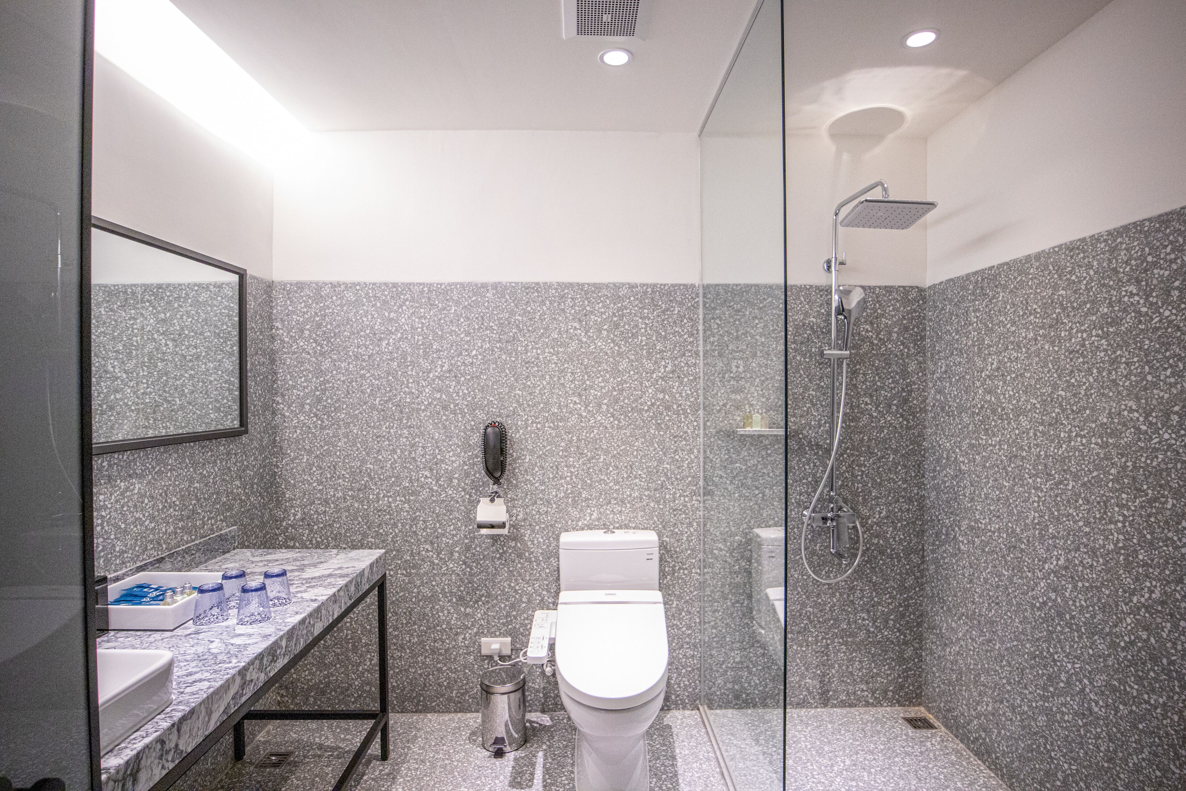 Casa de banho moderna com bancada de mármore, sanita, chuveiro e zona de duche separada por vidro.