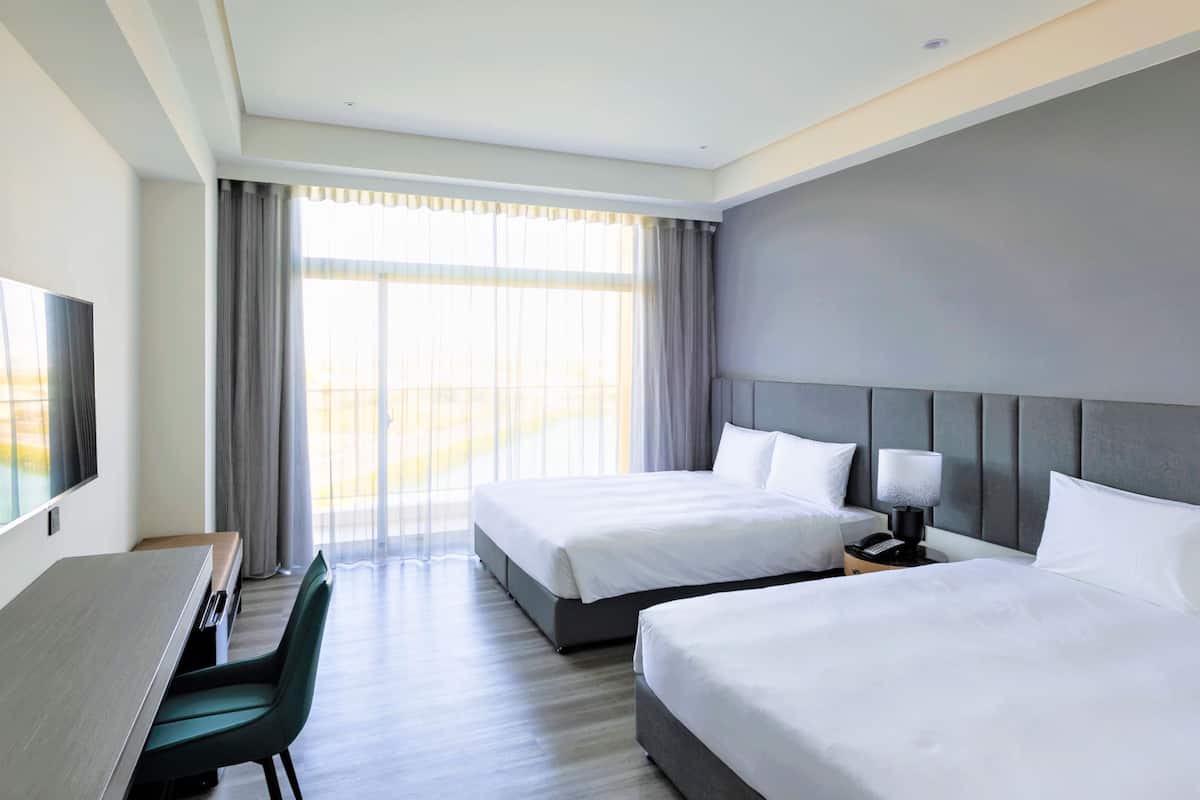 Quarto de hotel com duas camas, uma escrivaninha e uma televisão.