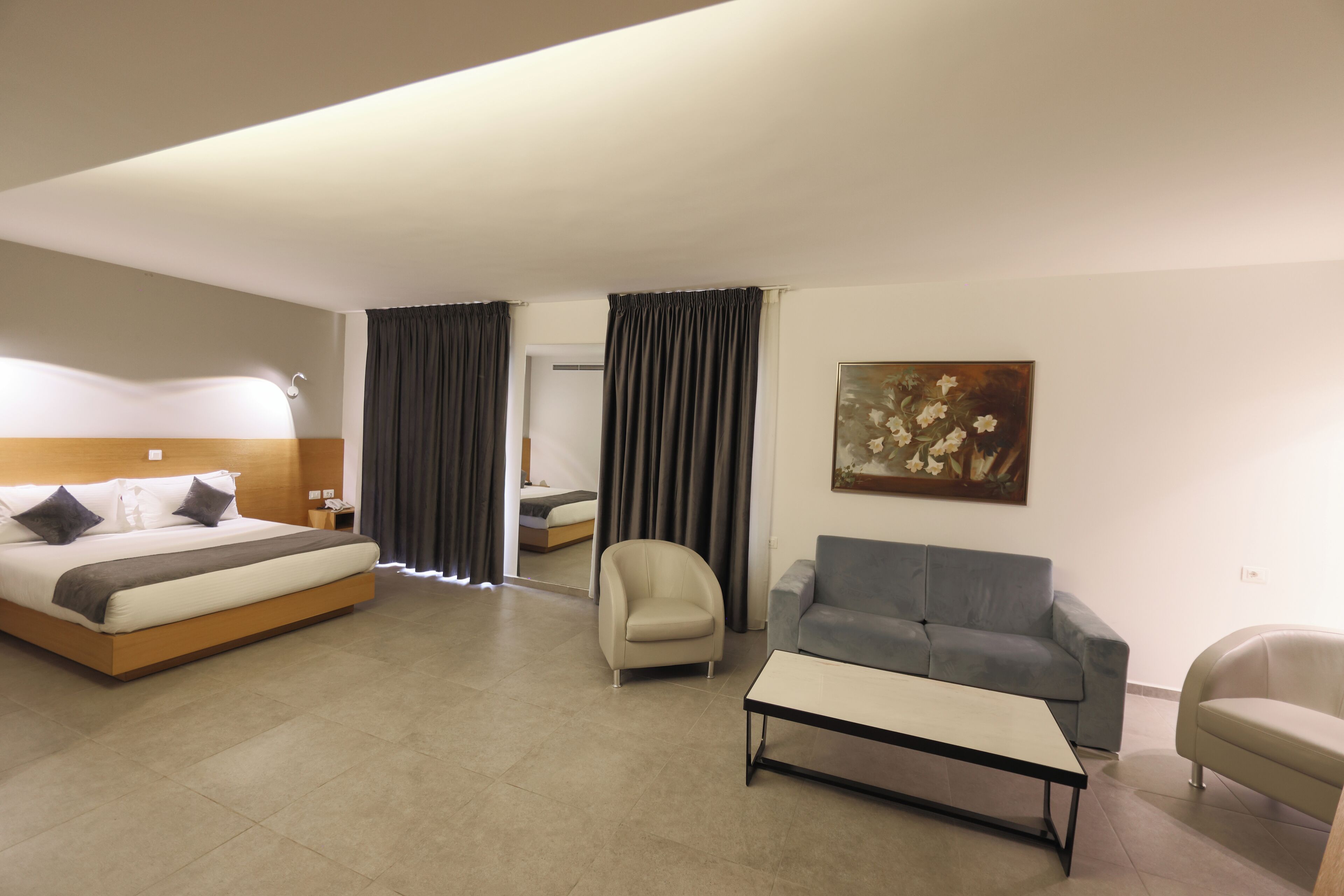 Quarto de hotel moderno com uma cama, um sofá, uma poltrona e uma mesa de centro.