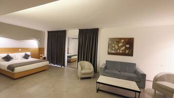 Quarto de hotel moderno com uma cama, um sofá, uma poltrona e uma mesa de centro.