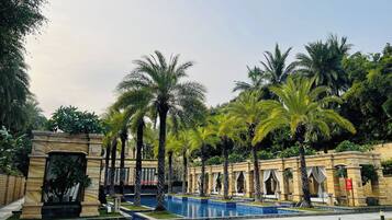 Uma área de piscina com palmeiras, um edifício de pedra e uma pequena estátua.