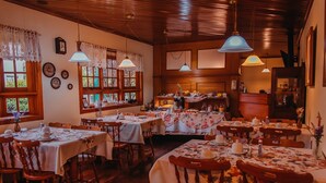 Um restaurante acolhedor com interiores em madeira, várias mesas preparadas para refeições e grandes janelas que permitem a entrada de luz natural.