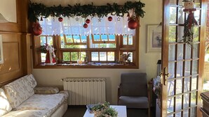 Uma sala de estar aconchegante com teto de madeira, um sofá, uma mesa com uma planta e uma janela decorada para o Natal.