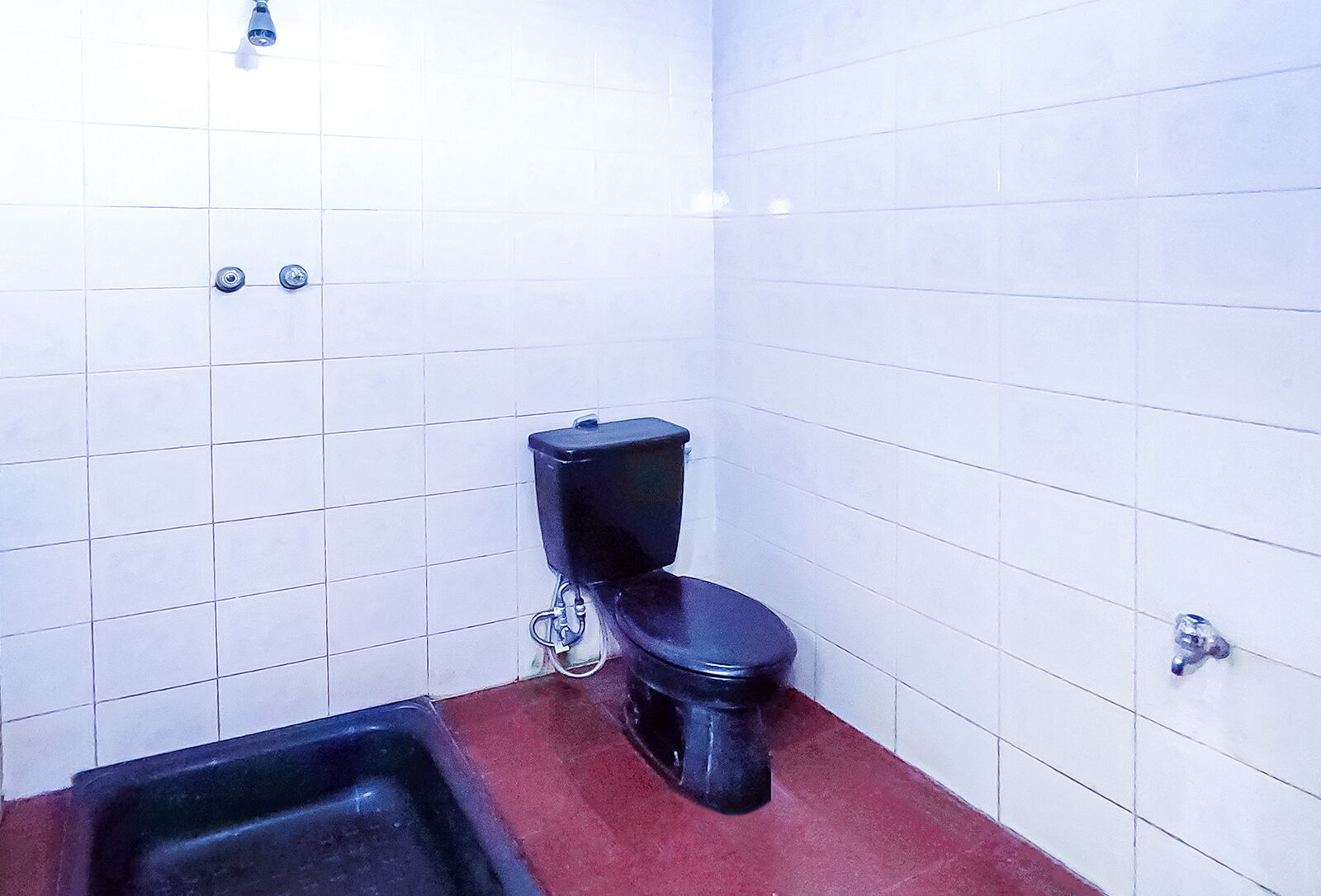 Casa de banho pequena, com azulejos, vaso sanitário preto, lavatório e chão vermelho.