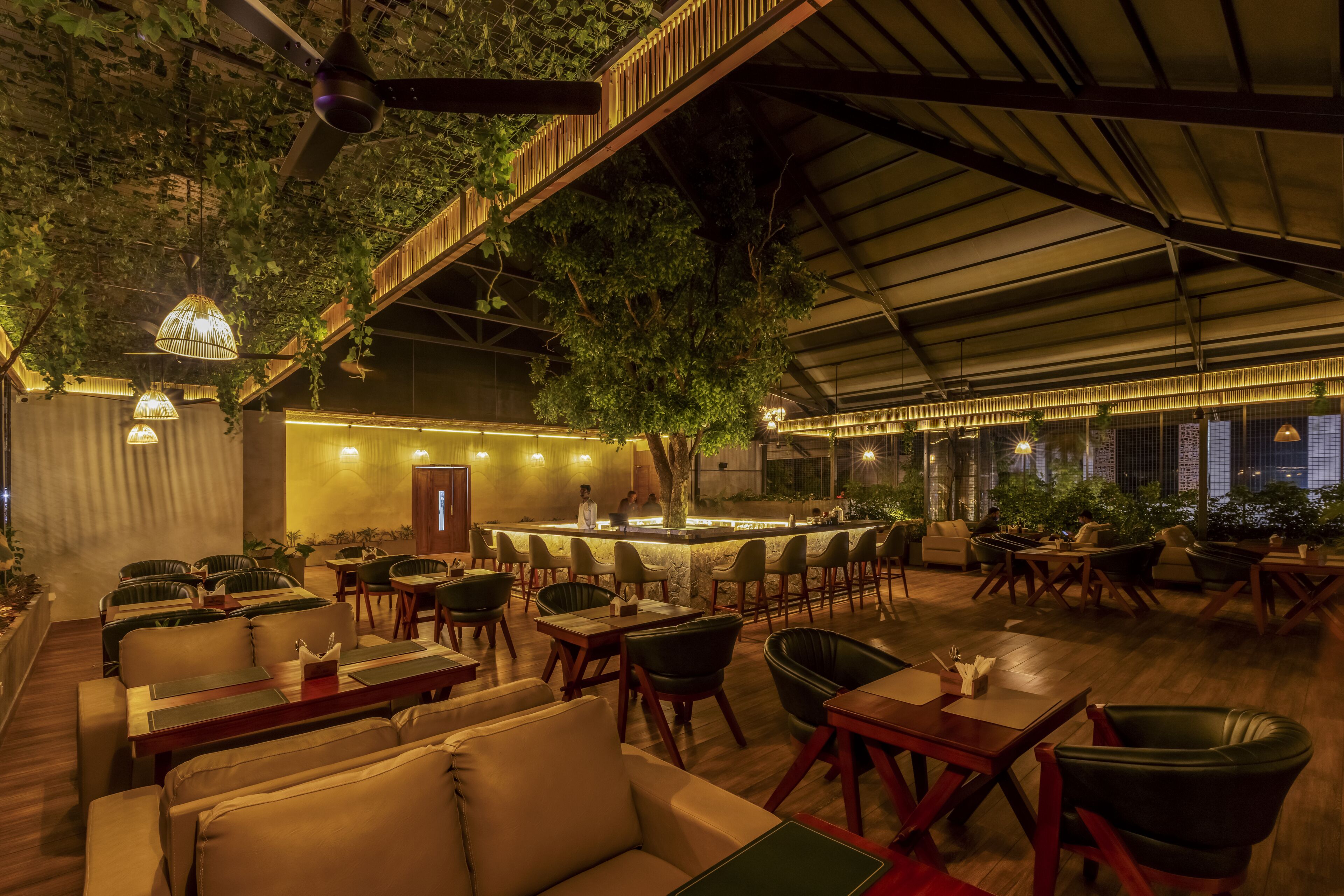 Um restaurante com teto alto, plantas penduradas e um espaço de bar.