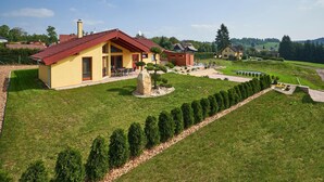 Uma casa amarela com telhado vermelho, rodeada por um gramado bem cuidado e uma fileira de árvores perenes.