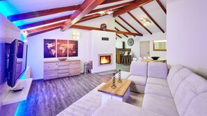 Uma sala de estar moderna com lareira, vigas de madeira, um sofá e uma televisão.