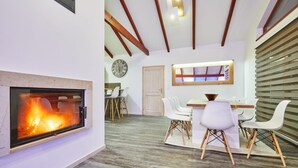 Uma sala de jantar moderna com lareira, vigas de madeira e uma mesa redonda com cadeiras brancas.