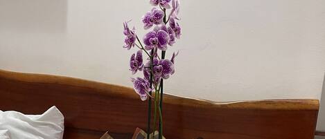 Um bolo branco com flores rosa e brancas sobre uma mesa branca em um quarto com cabeceira de madeira.