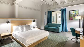 Quarto de hotel com uma cama grande, escrivaninha, cadeira, sofá e um quadro na parede.