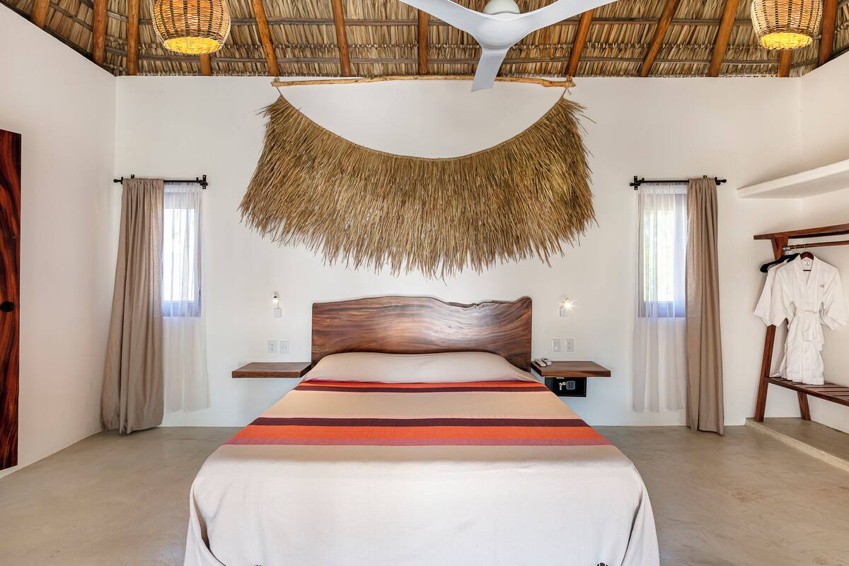 Um quarto espaçoso com uma cama grande, um ventilador de teto e um detalhe decorativo tecido no teto.