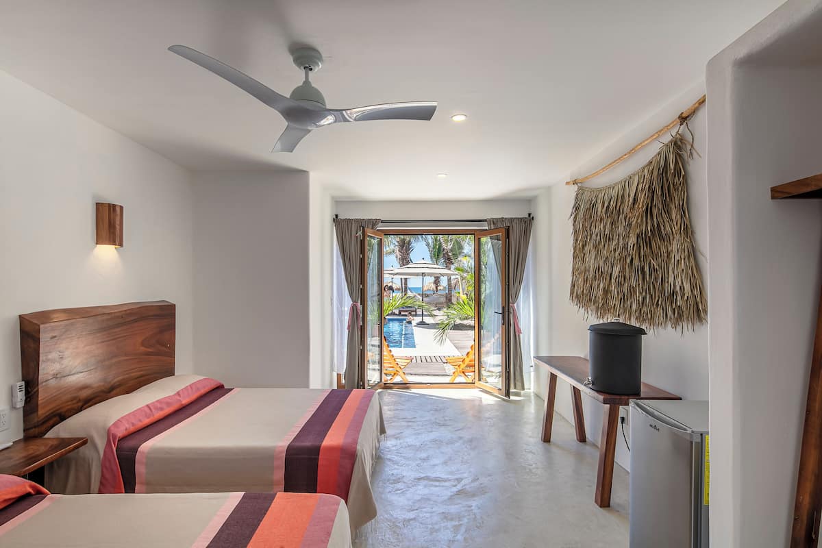 Quarto de hotel com duas camas, ventilador de teto, vista para uma piscina ao ar livre e um frigorífico.