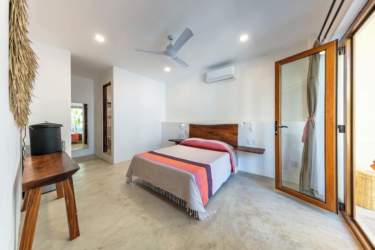 Quarto com cama, ventoinha no teto, aparelho de ar condicionado e porta de vidro deslizante.