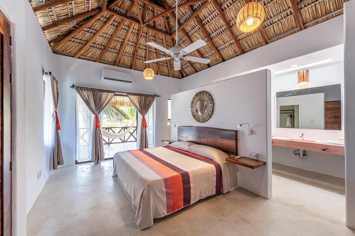 Quarto com cama, ventilador de teto, espelho grande e janela com cortinas.