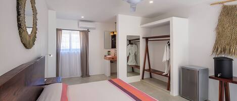 Quarto de hotel com cama, ventoinha no teto, guarda-roupa, mini-frigorífico e espelho na parede.