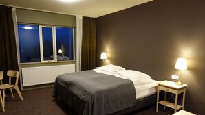 Quarto de hotel com cama, duas mesas de cabeceira com luminárias, uma cadeira e janela com cortinas.