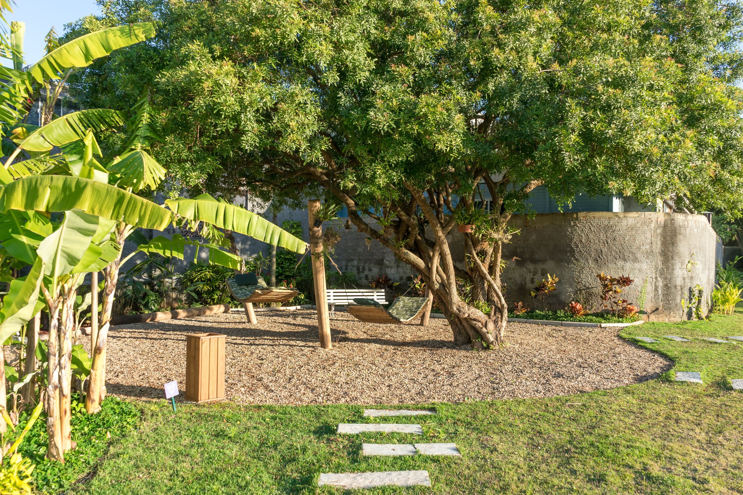 Um jardim com um banco, uma árvore e um caminho de pedra.