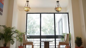 Um hall amplo com duas cadeiras voltadas para uma janela grande, uma mesa central e plantas em vasos.