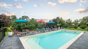 Uma piscina retangular com deck ladrilhado, rodeada por espreguiçadeiras e guarda-sóis.