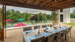 Uma área de refeições coberta ao ar livre, com vista para uma piscina e vegetação.