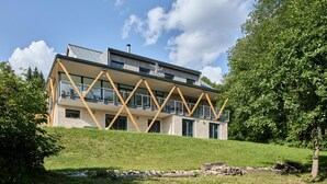 Uma casa moderna de dois andares com uma estrutura de telhado triangular única, grandes janelas e uma varanda com corrimão.