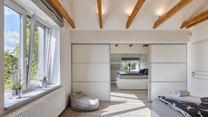 Quarto moderno com uma janela grande, cama com colcha listrada em preto e branco, poltrona de grão cinza e porta deslizante que dá para outro cômodo.