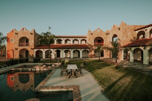 Um pátio com piscina, área de estar externa e um edifício com arcos e varandas.
