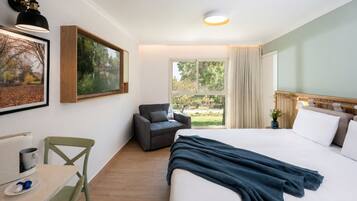 Quarto de hotel com cama, escrivaninha com cadeira, janela com cortinas e um quadro na parede.