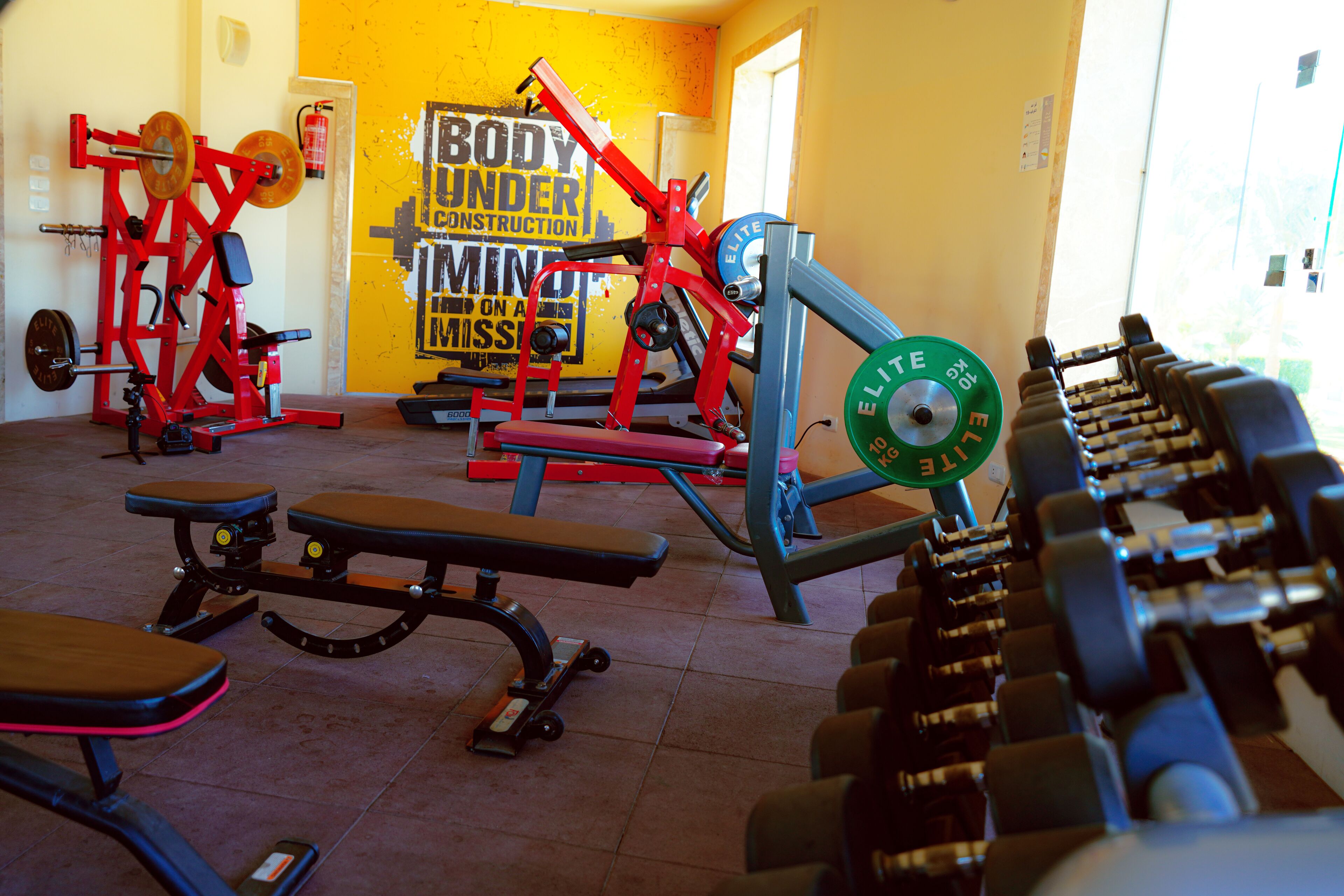 Academia com diversos equipamentos de exercício, incluindo bancos, halteres e máquinas de musculação.