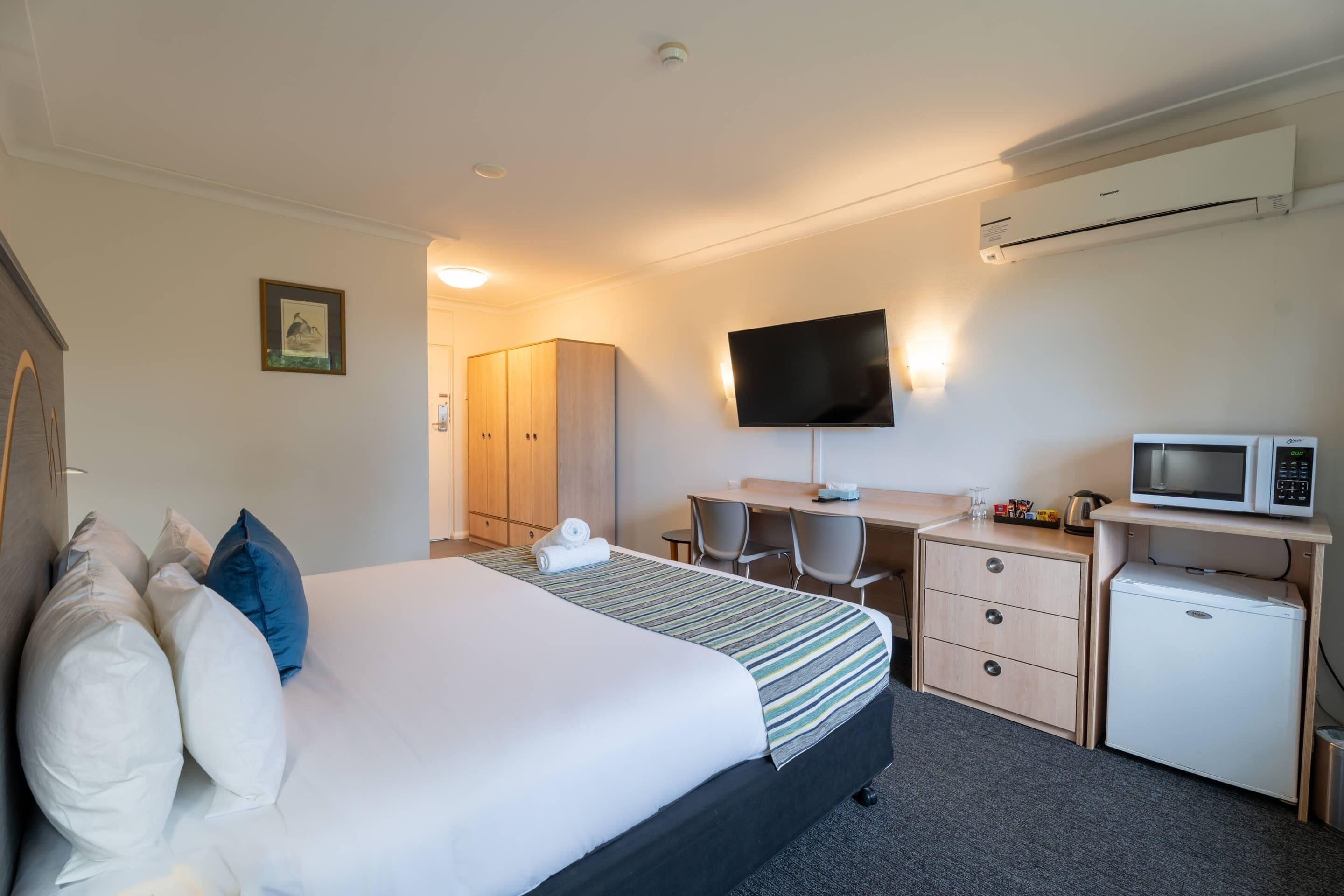 Quarto de hotel com cama, escrivaninha, televisão, micro-ondas e guarda-roupa.