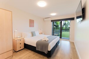 Quarto moderno com cama, mesas de cabeceira, guarda-roupa e porta de vidro deslizante para uma varanda.