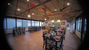 Uma sala de jantar espaçosa com várias mesas e cadeiras, janelas amplas e um teto alto com luminárias pendentes.