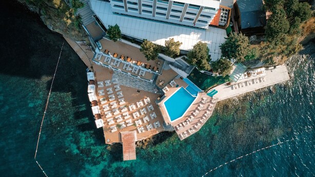 Vista aérea de um resort com piscina, espreguiçadeiras e um edifício com telhado ladrilhado.
