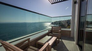 Varanda com guarda-corpo de vidro, vista para a água e uma linha de costa distante.
