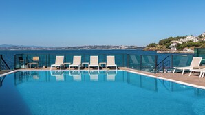 Piscina com espreguiçadeiras e vista para o mar e as colinas.