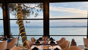 Mesa de jantar posta para quatro pessoas, com vista para o mar e montanhas.