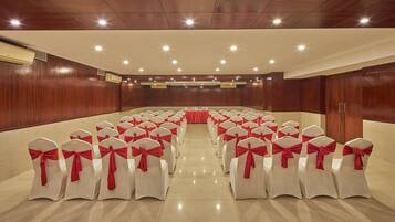 Uma sala de conferência com fileiras de cadeiras brancas com fitas vermelhas, painéis de madeira nas paredes e iluminação embutida.