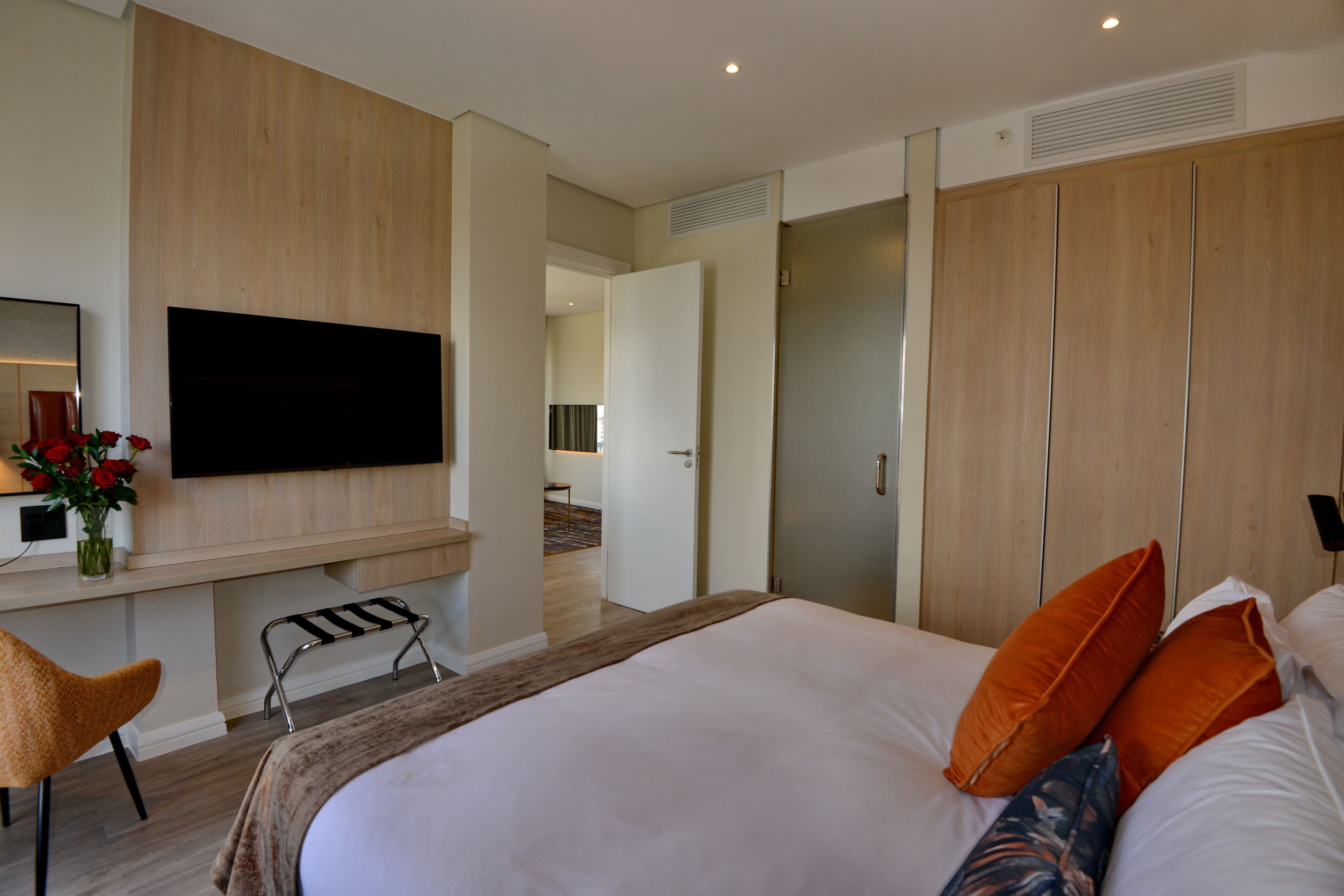 Quarto de hotel moderno com uma cama grande, uma televisão de tela plana na parede, uma escrivaninha com uma cadeira e um guarda-roupa.