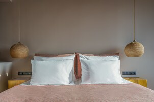 Cama bem arrumada com colcha estampada, duas almofadas brancas e cabeceira de tecido trançado.