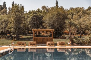 Uma área de piscina com espreguiçadeiras de madeira e um pérgola.