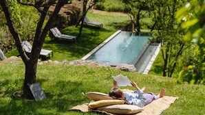 Uma pessoa deitada em um cobertor perto de uma piscina, lendo um livro.