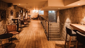 Um restaurante com pisos de madeira, paredes de pedra e uma escada que leva a um andar superior.
