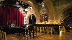 Uma área de bar com palco, banquetas e uma parede de pedra.