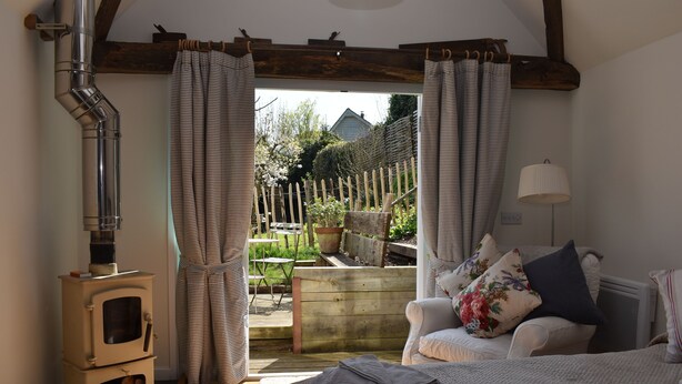 Quarto aconchegante com cama de madeira, um pequeno aquecedor e vista para um jardim através de uma janela com cortinas.