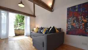 Uma sala de estar com um sofá cinzento, uma pintura abstrata colorida e piso de madeira.