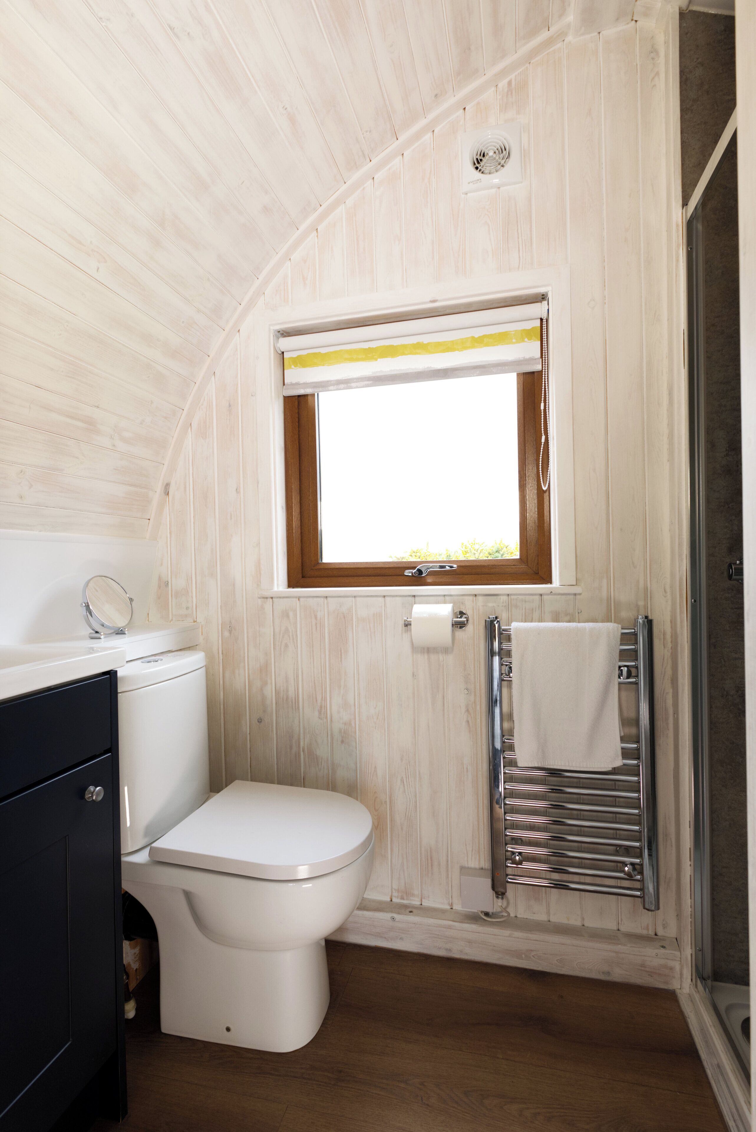Uma casa de banho compacta com sanita, porta-toalhas, janela e zona de duche.