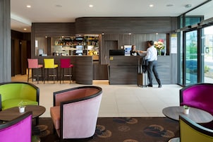 Um hall de hotel moderno com balcão de recepção, área de bar e assentos coloridos.